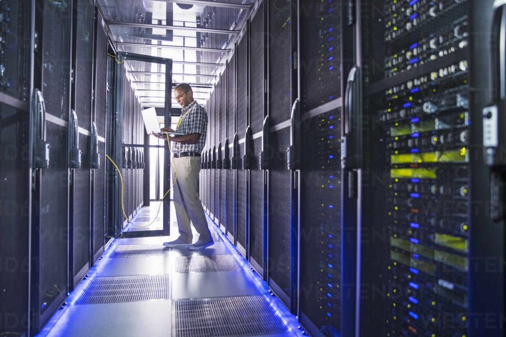 Technician with laptop working at mainframe computers in data center ...